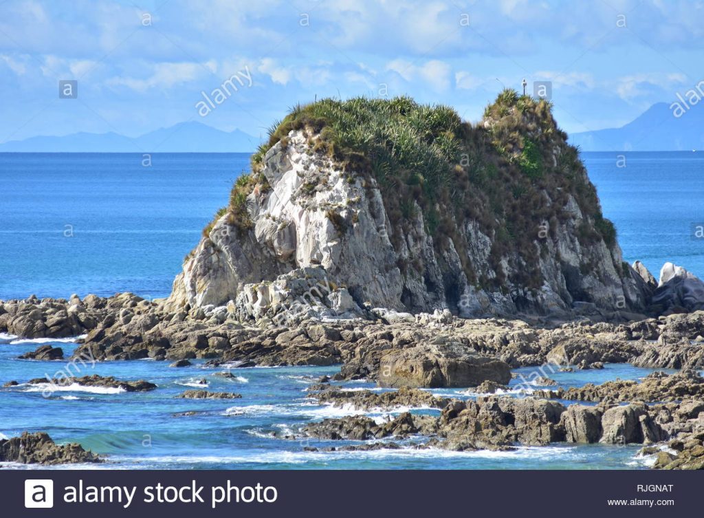 Large rock formation in blue sea near sea shore eroding under elements ...